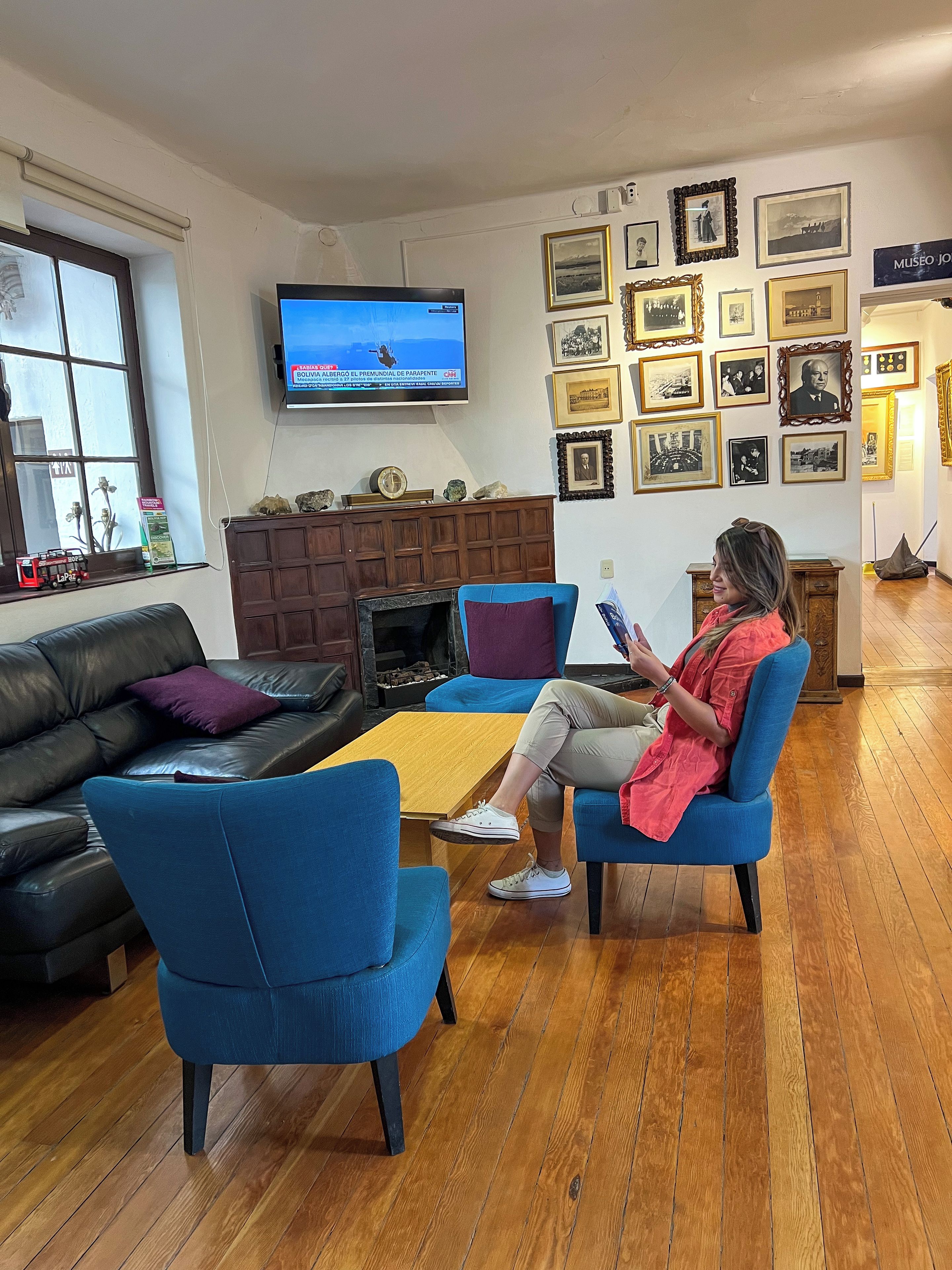 Uma sala de estar com televisão, poltronas azuis, um sofá de couro preto e lareira.