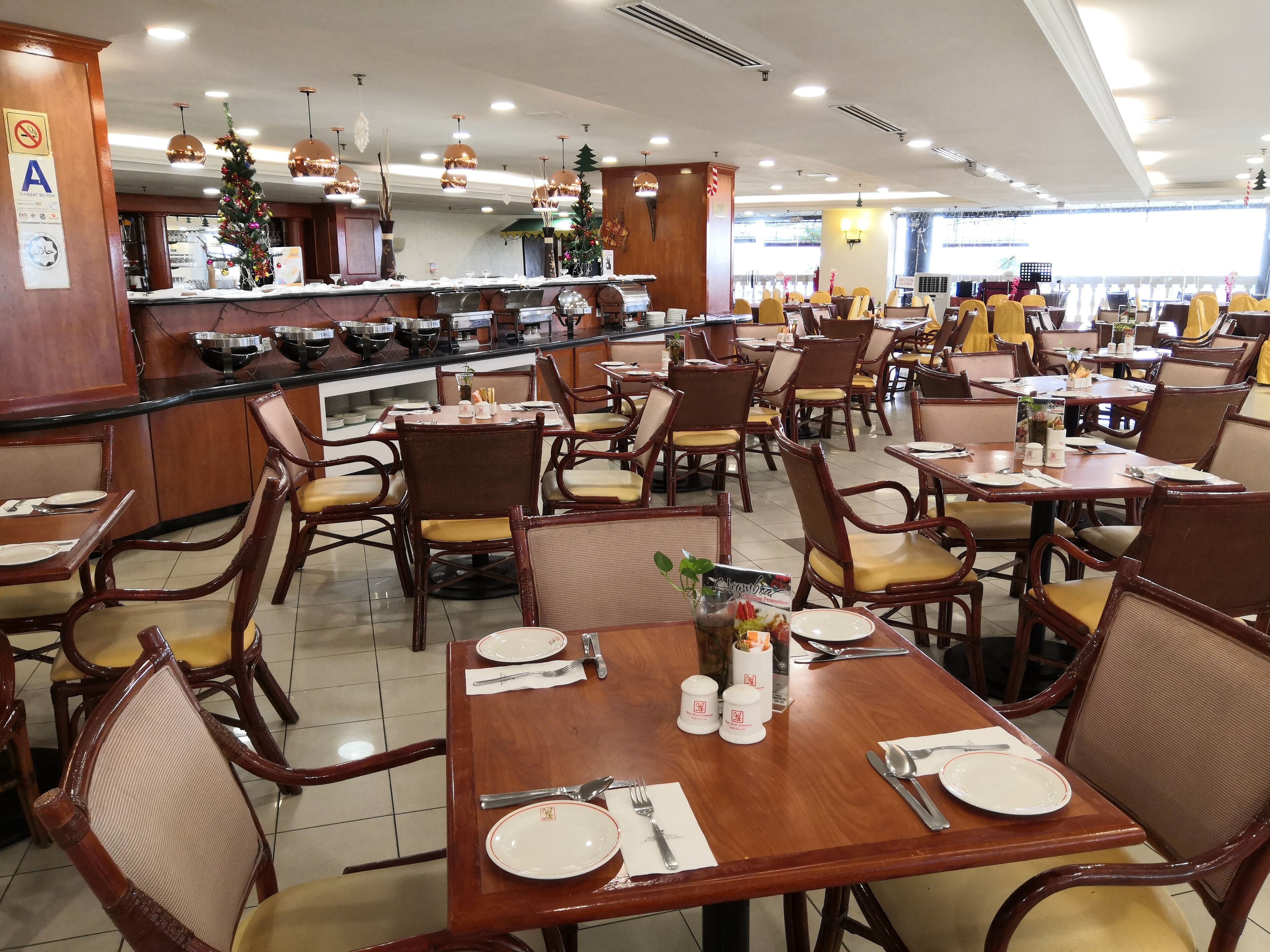 Um restaurante espaçoso com mesas e cadeiras de madeira, um balcão central e vista para a rua.