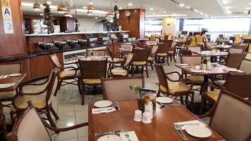 Um restaurante espaçoso com mesas e cadeiras de madeira, um balcão central e vista para a rua.