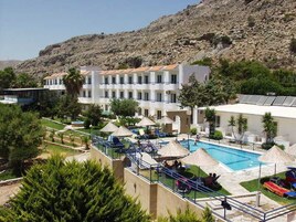 Um hotel com piscina, espreguiçadeiras e montanhas ao fundo.