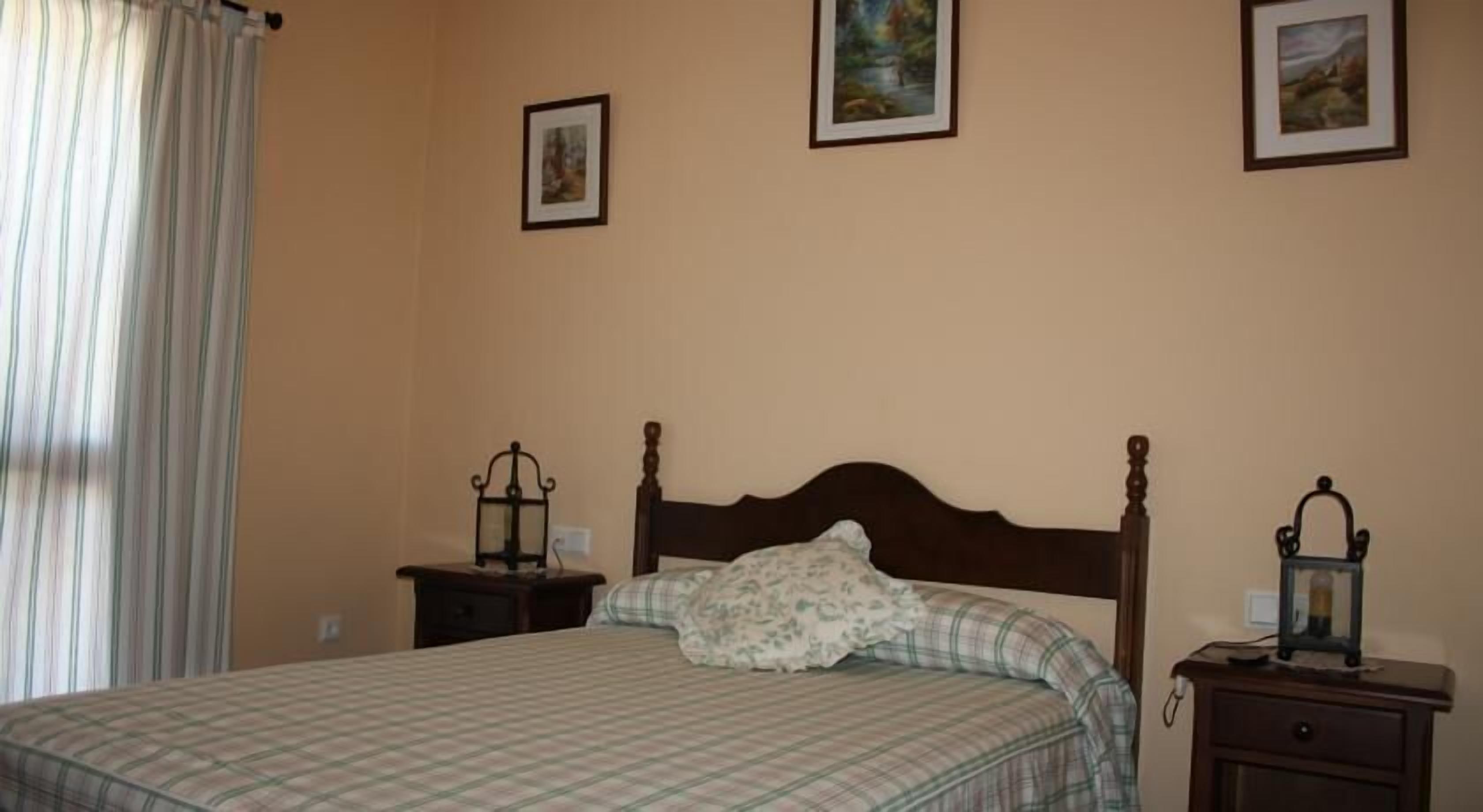 Quarto com uma cama, duas mesas de cabeceira e duas luminárias fixadas na parede.