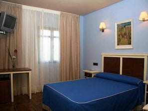 Quarto de hotel com cama, escrivaninha, televisão e um quadro na parede.