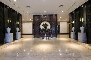 Um hall amplo com piso de mármore, área de estar central com mesa e cadeiras, e vasos decorativos em ambos os lados.