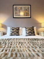 Quarto com cama, almofadas, um quadro na parede e abajures.