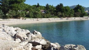 Uma costa rochosa com águas cristalinas, árvores e edifícios ao fundo.