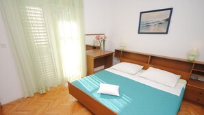 Quarto com cama, cabeceira de madeira, mesas de cabeceira, mesa de apoio, abajur e um quadro na parede.