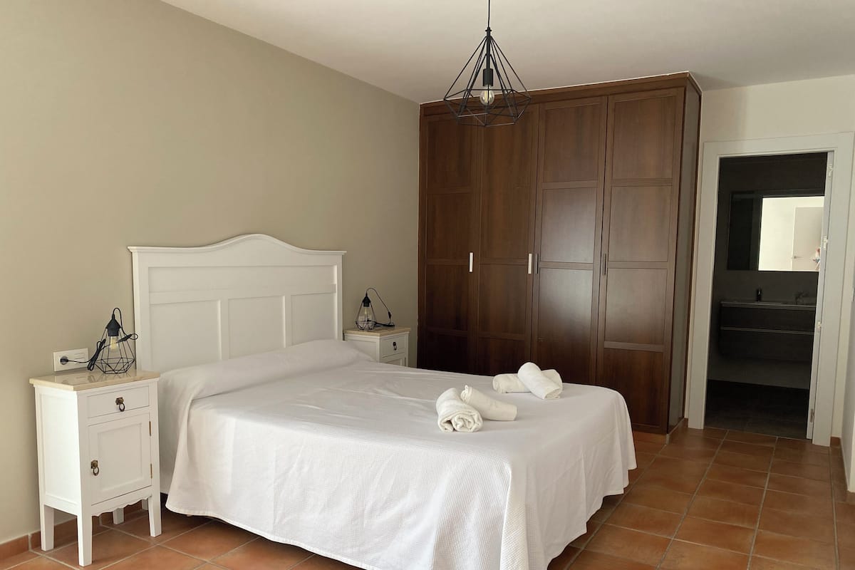 Quarto com cama, mesas de cabeceira, guarda-roupa e luminária pendente.
