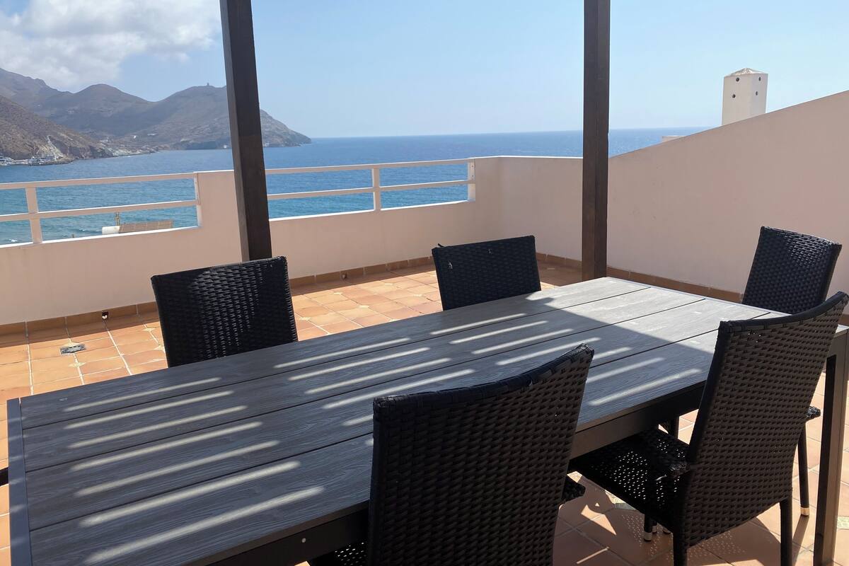 Terraço com mesa e cadeiras, vista para a costa, montanhas e o mar.