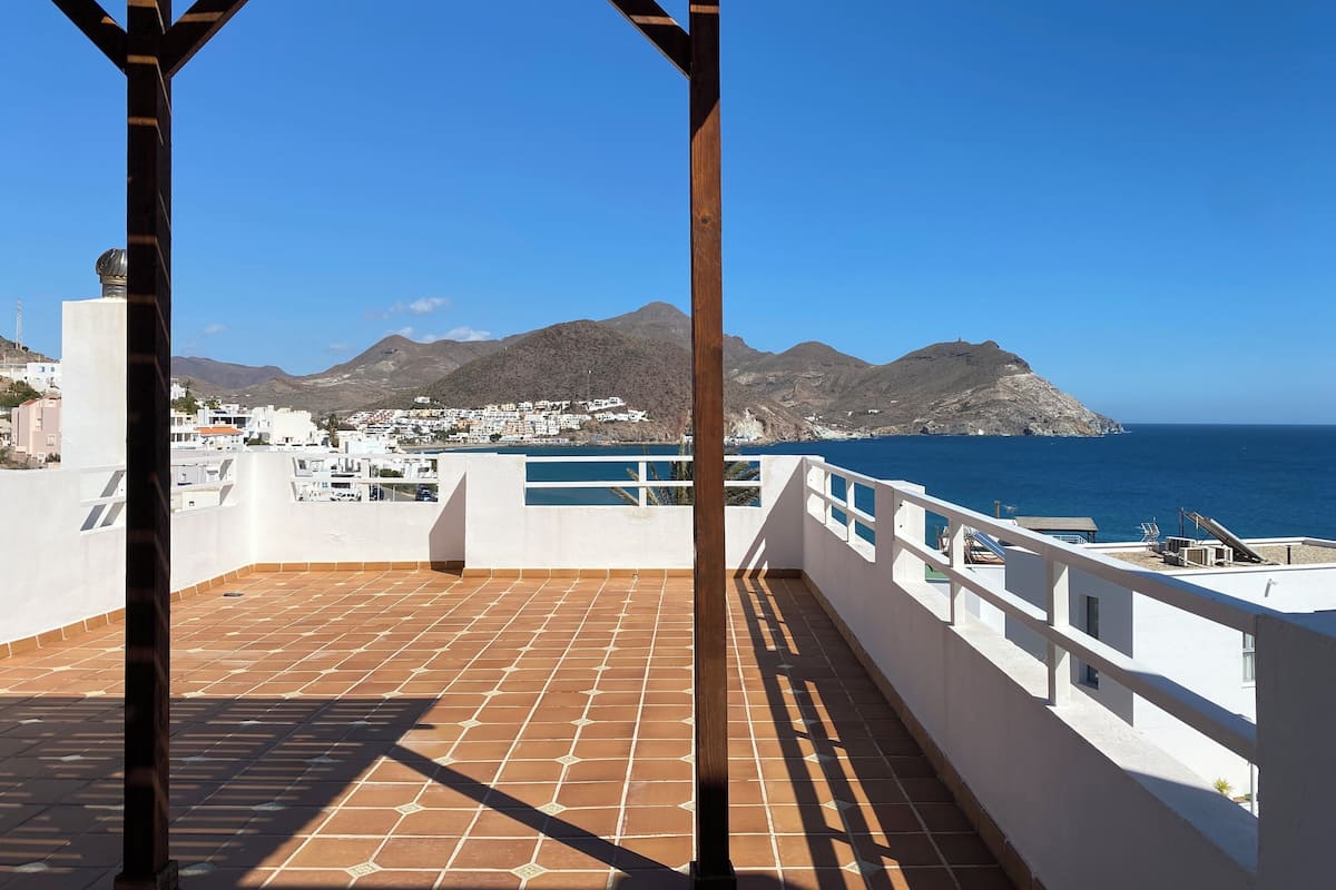Terraço com vista para o mar e montanhas, com estrutura de pérgula.