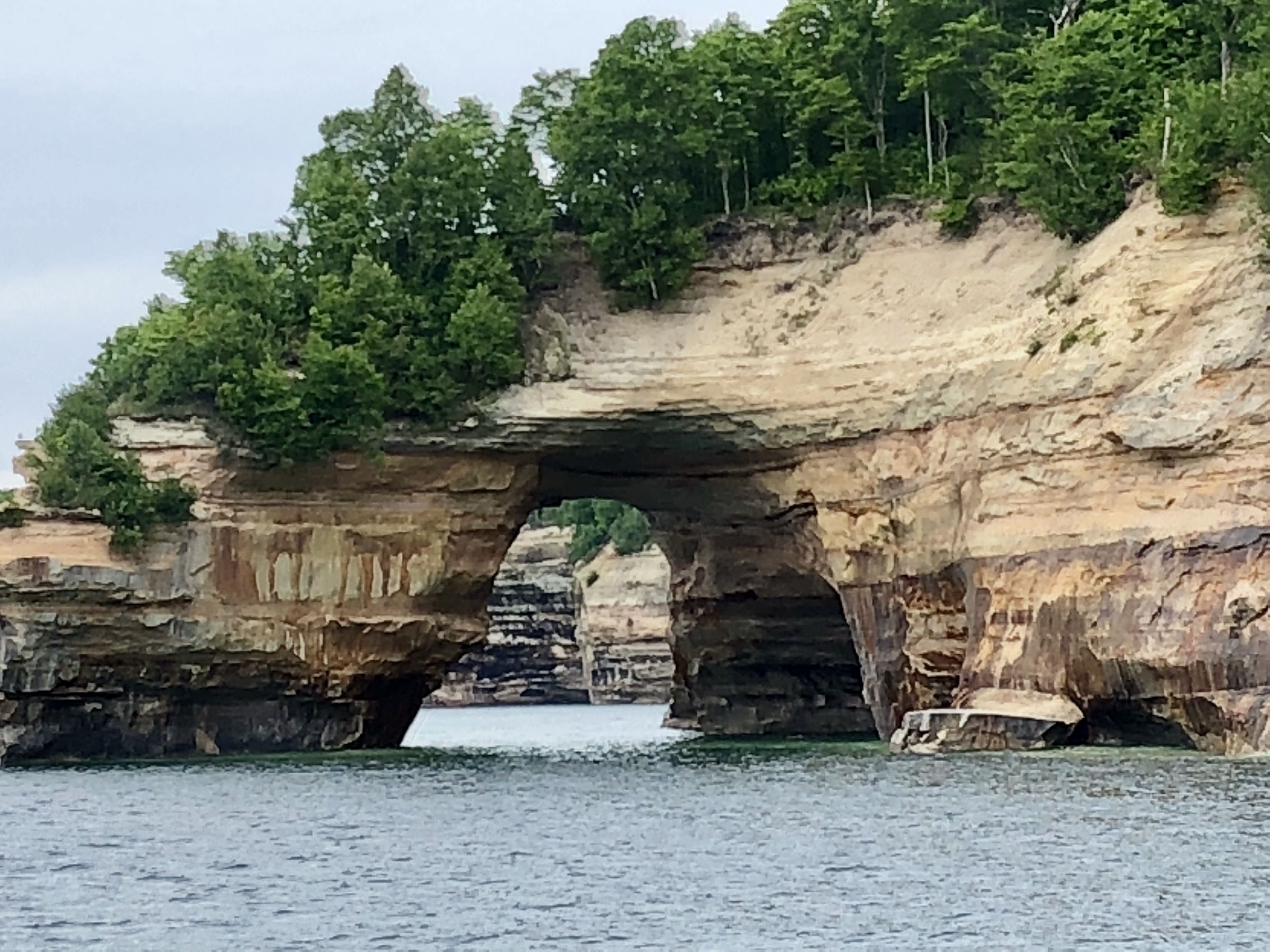 Formação rochosa natural em arco sobre a água, rodeada por vegetação.