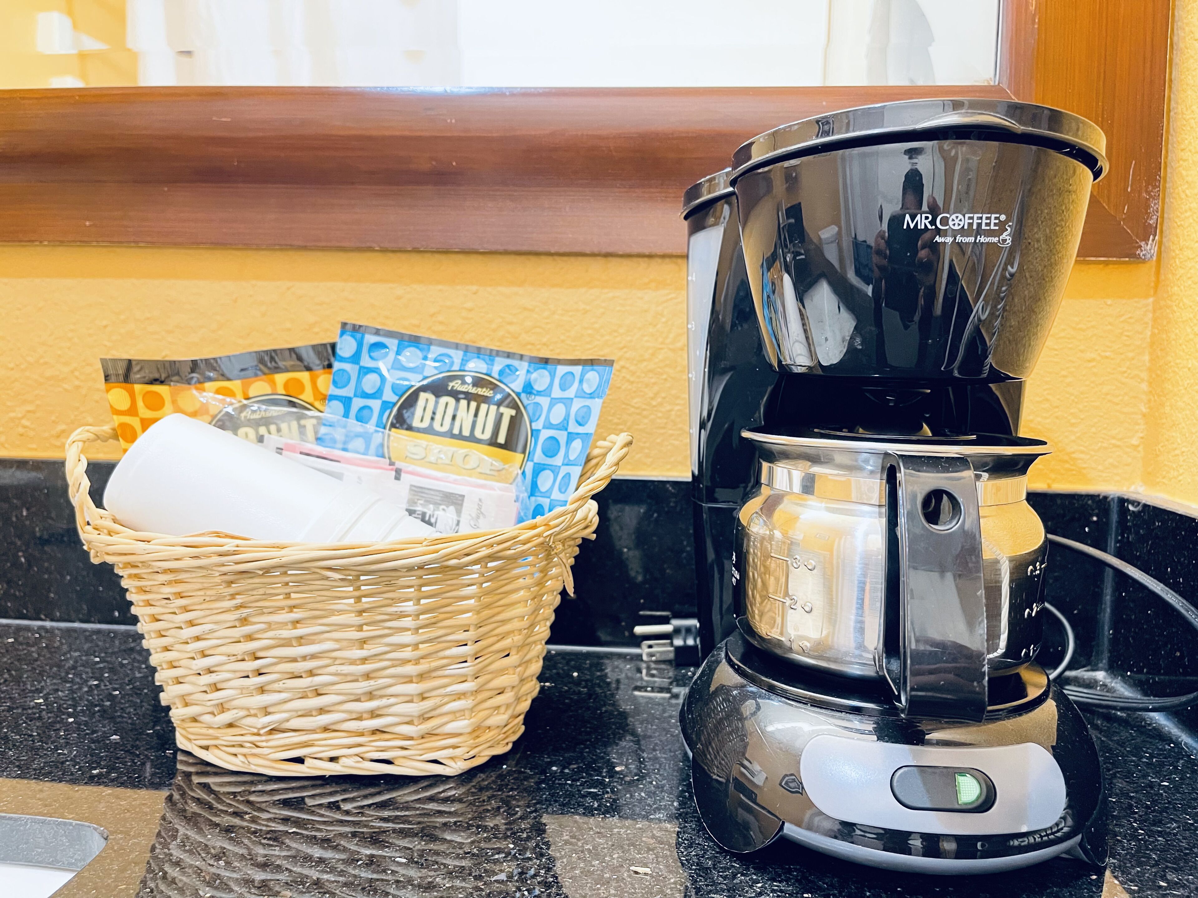 Máquina de café com uma cesta contendo um saco de donuts, um saco de café e um jornal.