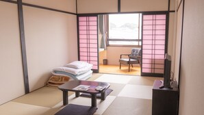 Um quarto japonês tradicional, com piso de tatame, futon, mesa com revistas e TV sobre um suporte.