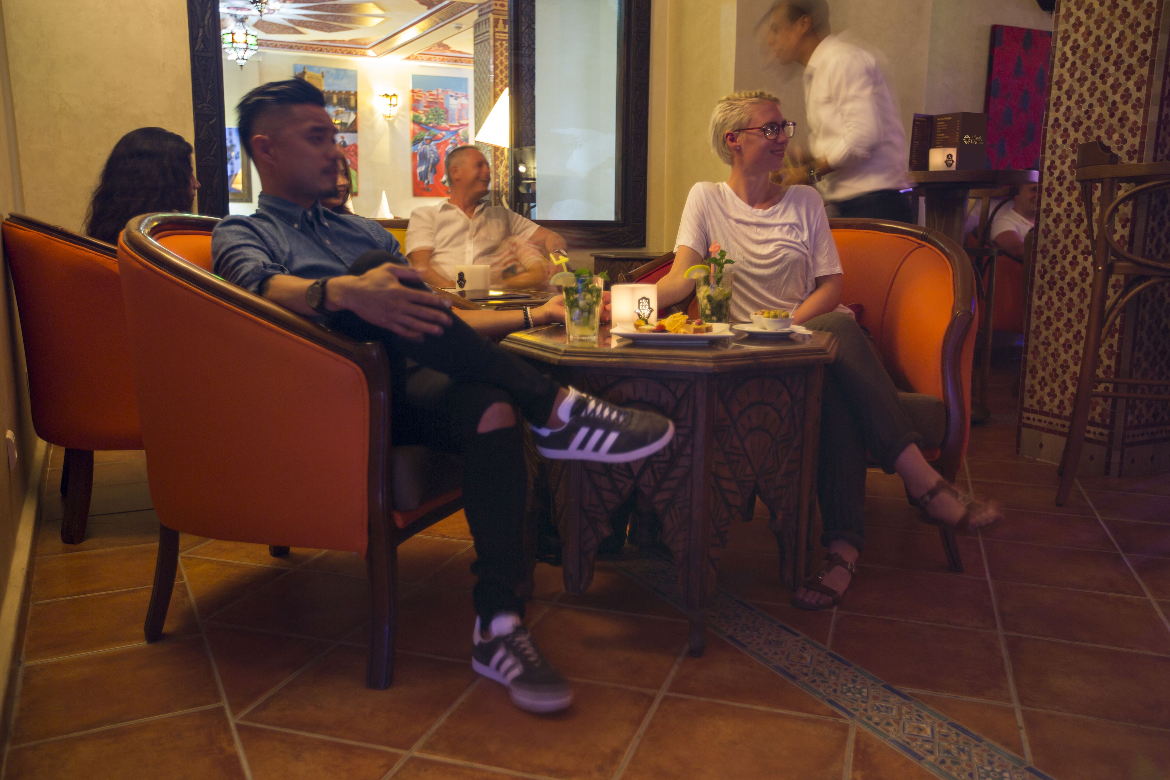 Restaurante com cadeiras laranja e chão de azulejos.