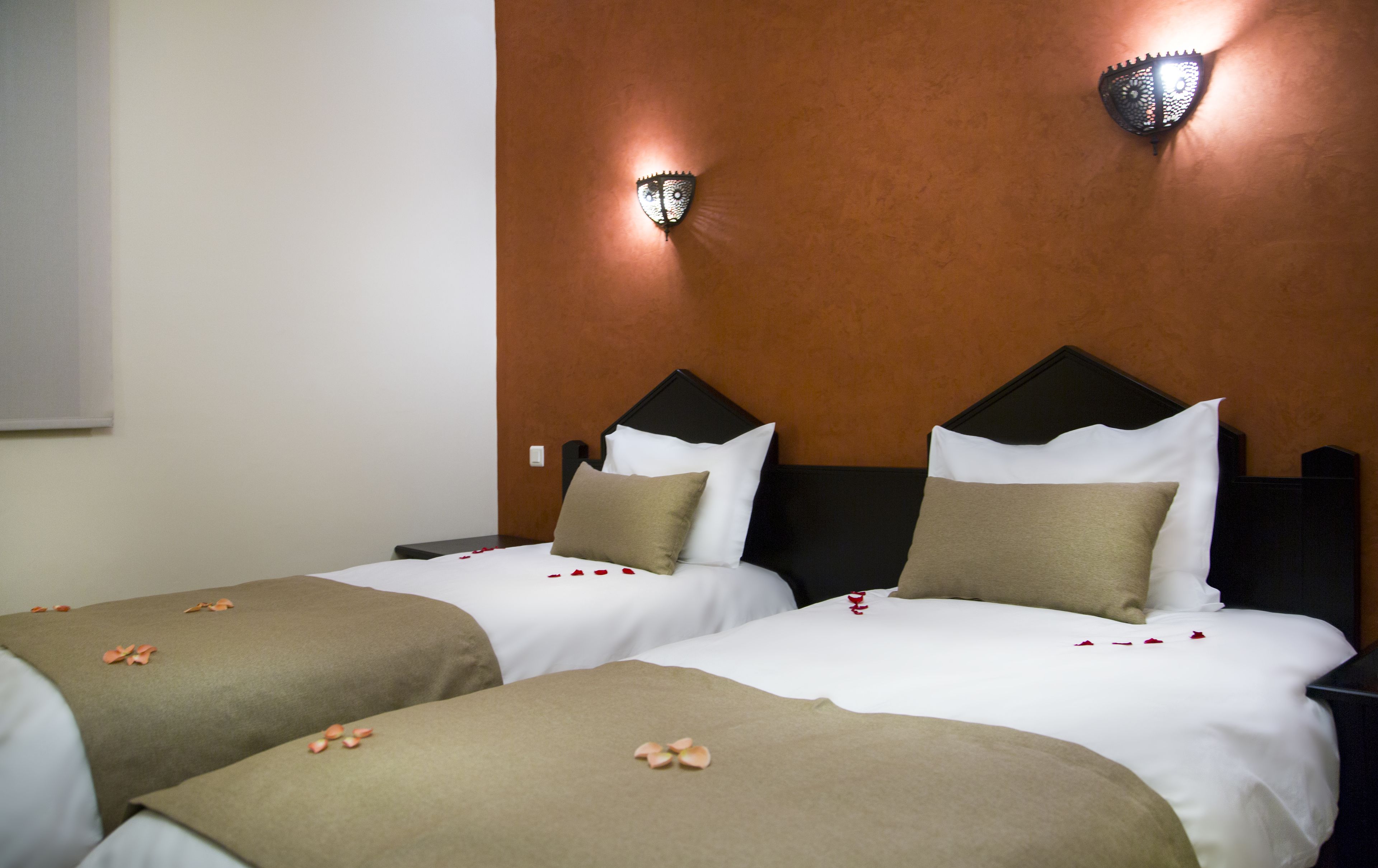 Quarto de hotel com duas camas, roupa de cama bege e branca, e pétalas de rosa sobre as camas.