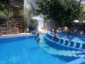Piscina com escadas de acesso, rodeada por espreguiçadeiras e guarda-sóis.