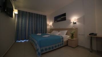Quarto de hotel com cama, mesa de cabeceira com telefone, televisão na parede e um quadro.