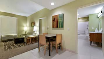 Quarto de hotel com área de jantar, sofá, luminária e pintura na parede.