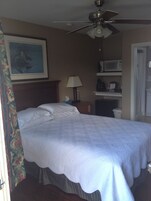 Quarto com cama, ventoinha no teto, pintura na parede, luminária e micro-ondas em uma prateleira.