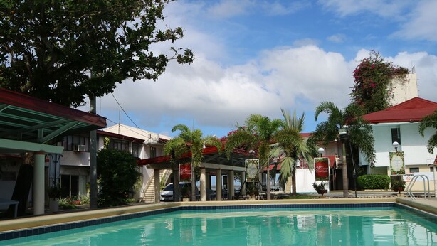 Piscina com borda azulejada, rodeada por edifícios com telhados vermelhos e alguma vegetação.