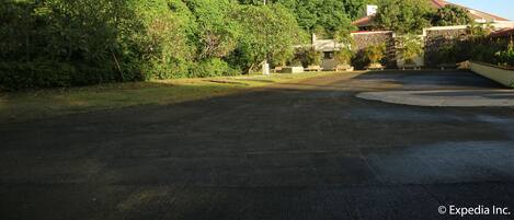 Uma área pavimentada com uma estátua numa colina, rodeada por vegetação e edifícios com telhados vermelhos.