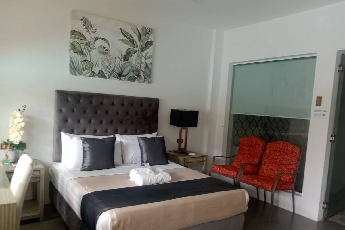 Quarto de hotel com uma cama, uma cadeira, uma escrivaninha e um quadro na parede.