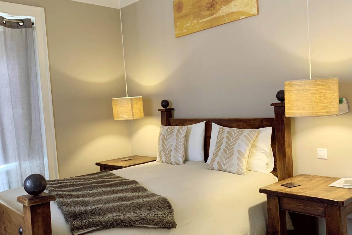 Uma cama bem arrumada com um tapete fofinho, mesas de cabeceira de madeira e um abajur.