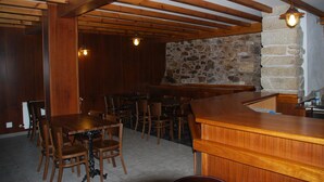 Restaurante com mesas e cadeiras de madeira, parede de pedra e teto de madeira com vigas aparentes.