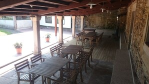 Um pátio ao ar livre com mesas e bancos de madeira, paredes de pedra e luminárias pendentes.