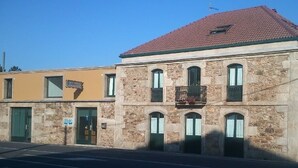 Um edifício de pedra com telhado de telhas vermelhas, uma varanda e uma placa indicando uma área de estacionamento.