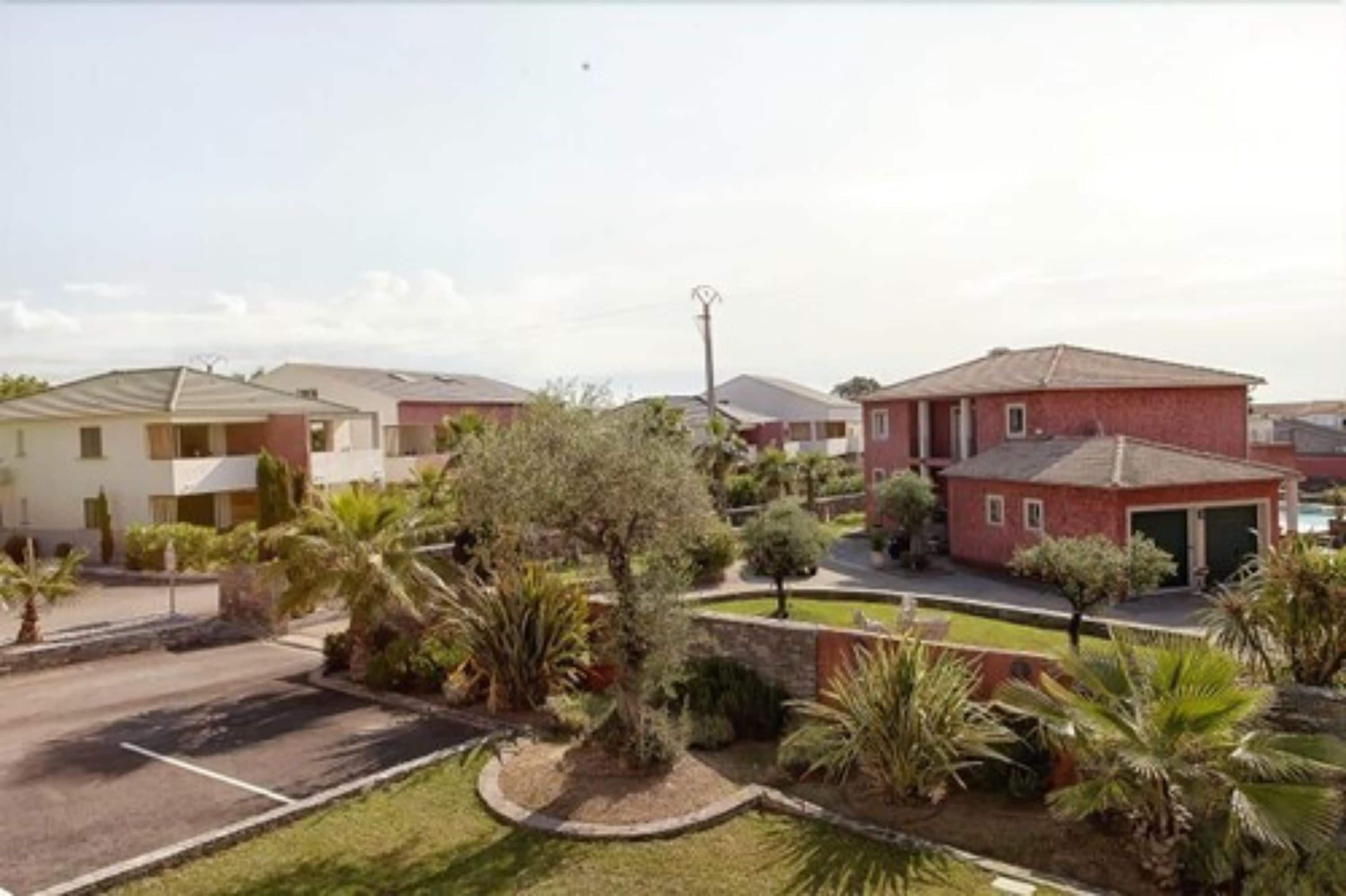 Uma área residencial com várias casas, um estacionamento e paisagismo bem cuidado, incluindo palmeiras e arbustos.