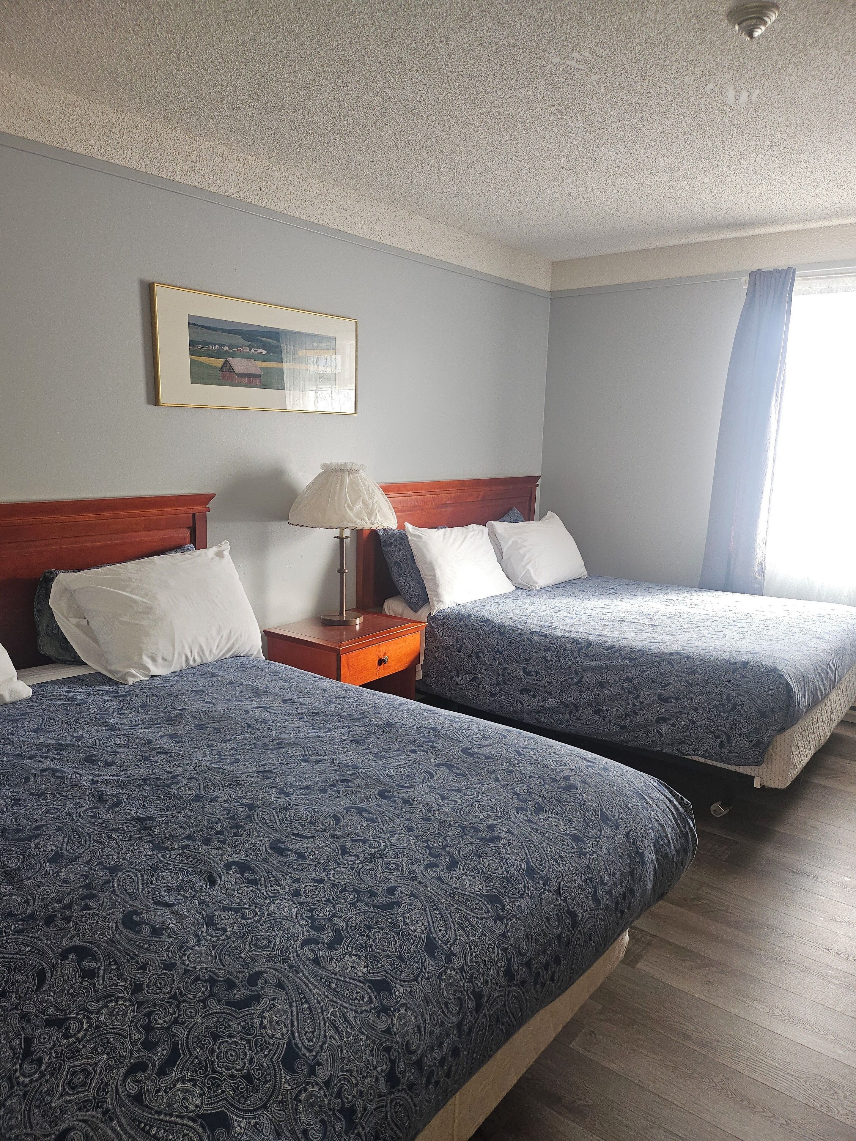 Quarto de hotel com duas camas, uma mesa de cabeceira, um abajur e um quadro na parede.