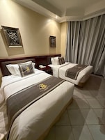 Quarto de hotel com duas camas, uma mesinha de cabeceira, um telefone e uma janela grande com cortinas.