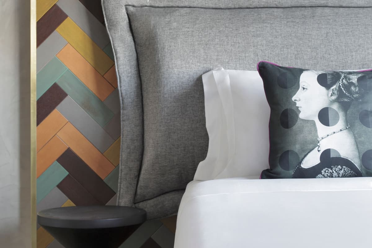 Quarto moderno com cabeceira em padrão herringbone, mesa de cabeceira preta e almofada decorativa.