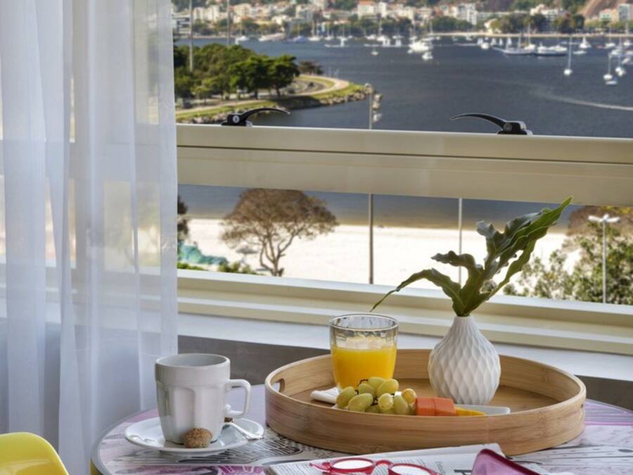 Mesa de jantar com itens de café da manhã, vista para montanha e um porto com barcos.