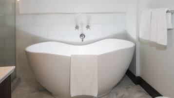Uma banheira em formato de coração com uma toalha pendurada, um vaso sanitário e um porta-toalhas num banheiro com azulejos brancos e piso de mármore.