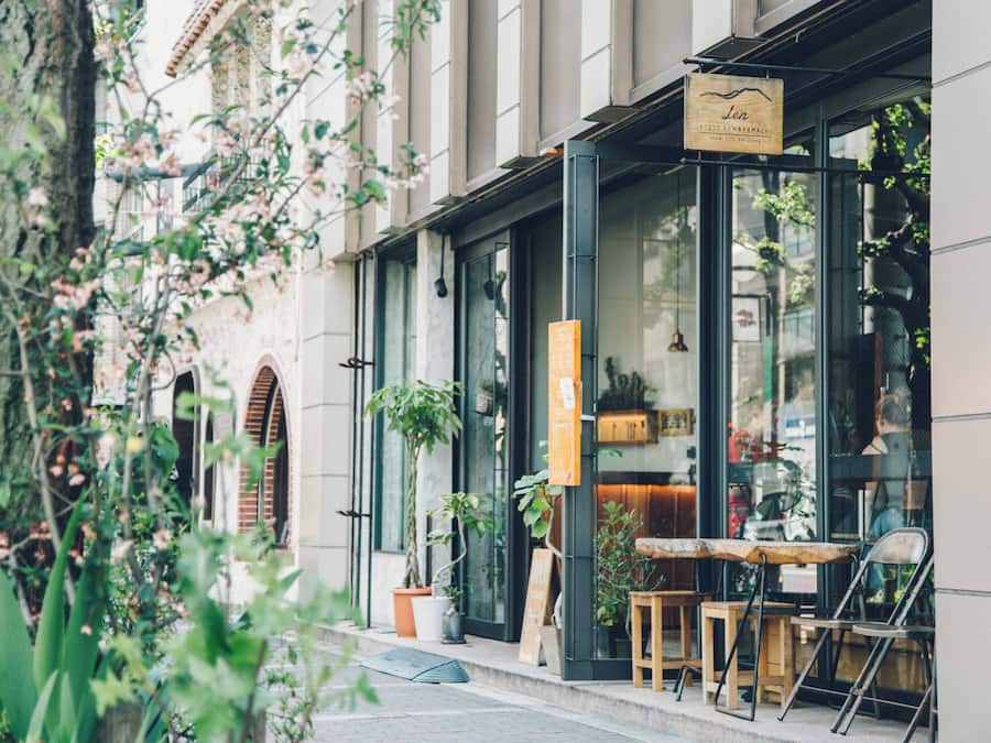 Um café com mesas ao ar livre, plantas em vasos e uma placa.