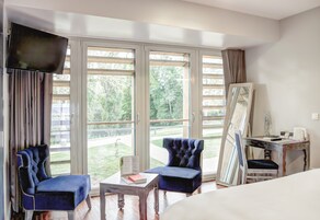 Quarto de hotel com uma cama grande, duas poltronas azuis, uma pequena mesa, escrivaninha com espelho e televisão.