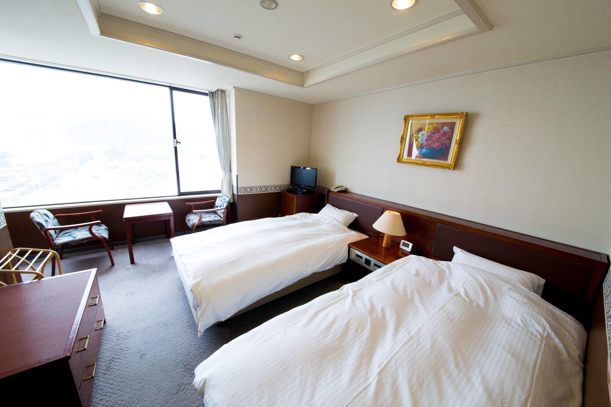 Quarto de hotel com duas camas, uma escrivaninha, uma cadeira, uma televisão e um quadro na parede.