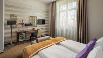 Quarto de hotel com cama, escrivaninha, computador, televisão e janela com cortinas.