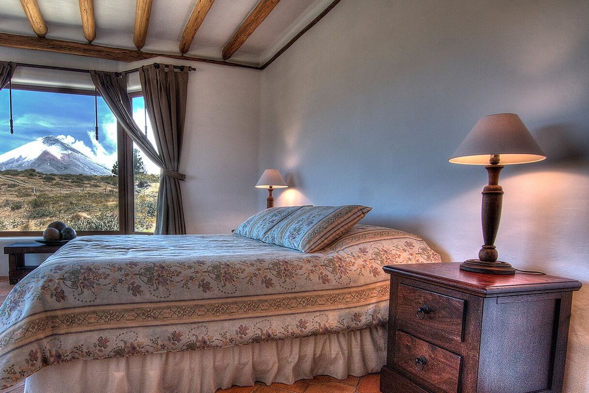 Quarto com uma cama, duas luminárias de cabeceira, uma mesa de cabeceira e vista para uma montanha.