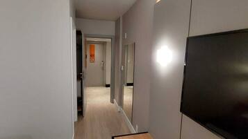 Quarto de hotel moderno com cama de madeira, escrivaninha, televisão de tela plana na parede e corredor que dá para o banheiro.