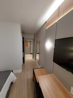 Quarto de hotel moderno com cama de madeira, escrivaninha, televisão de tela plana na parede e corredor que dá para o banheiro.