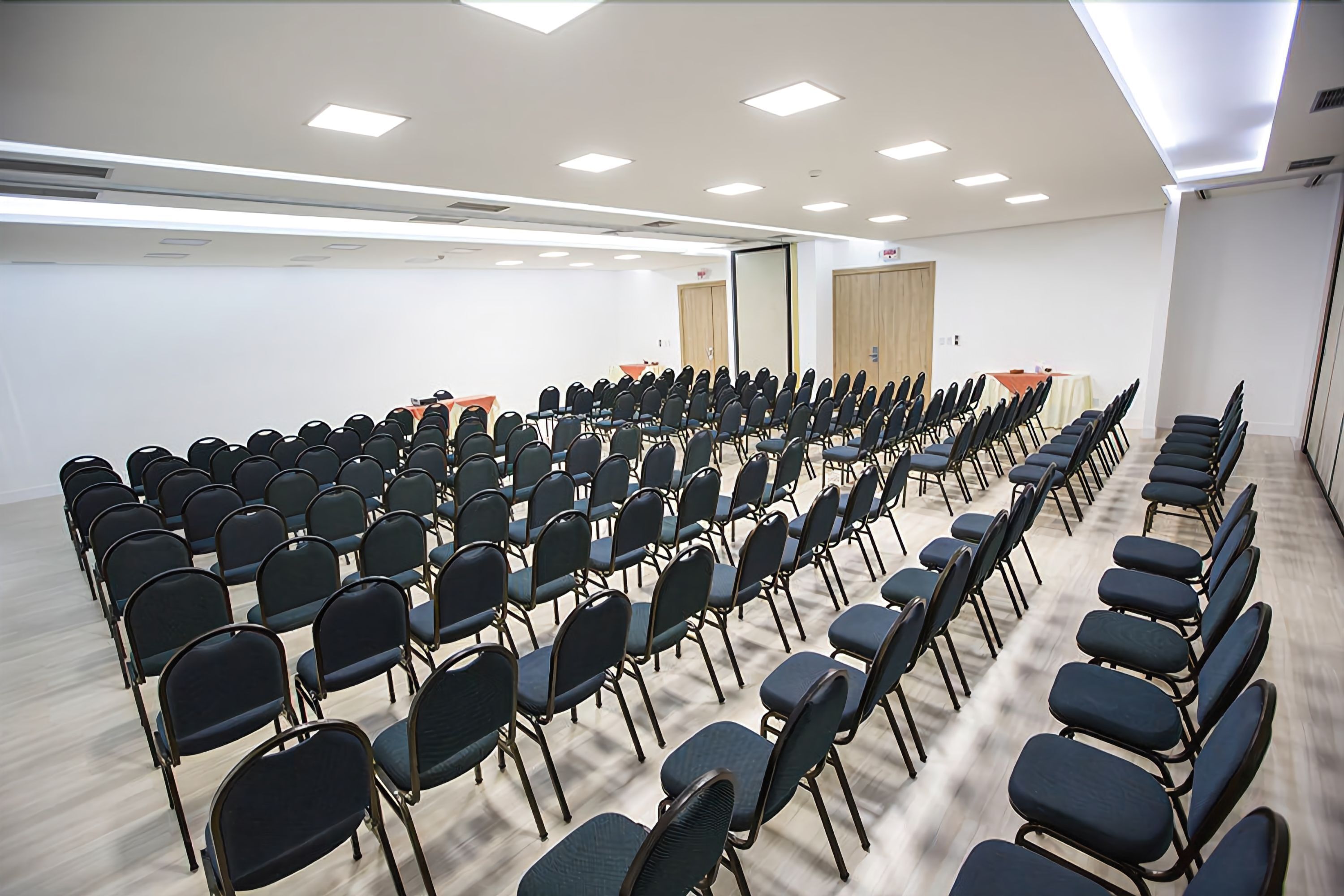 Uma sala de conferências com fileiras de cadeiras, um quadro branco e uma porta.