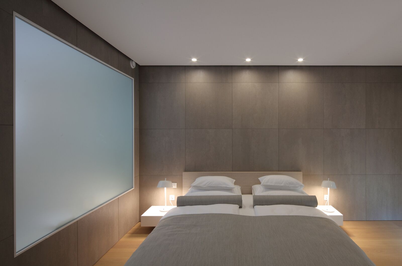 Quarto moderno com uma cama grande, duas mesas de cabeceira e uma tela de projeção na parede.