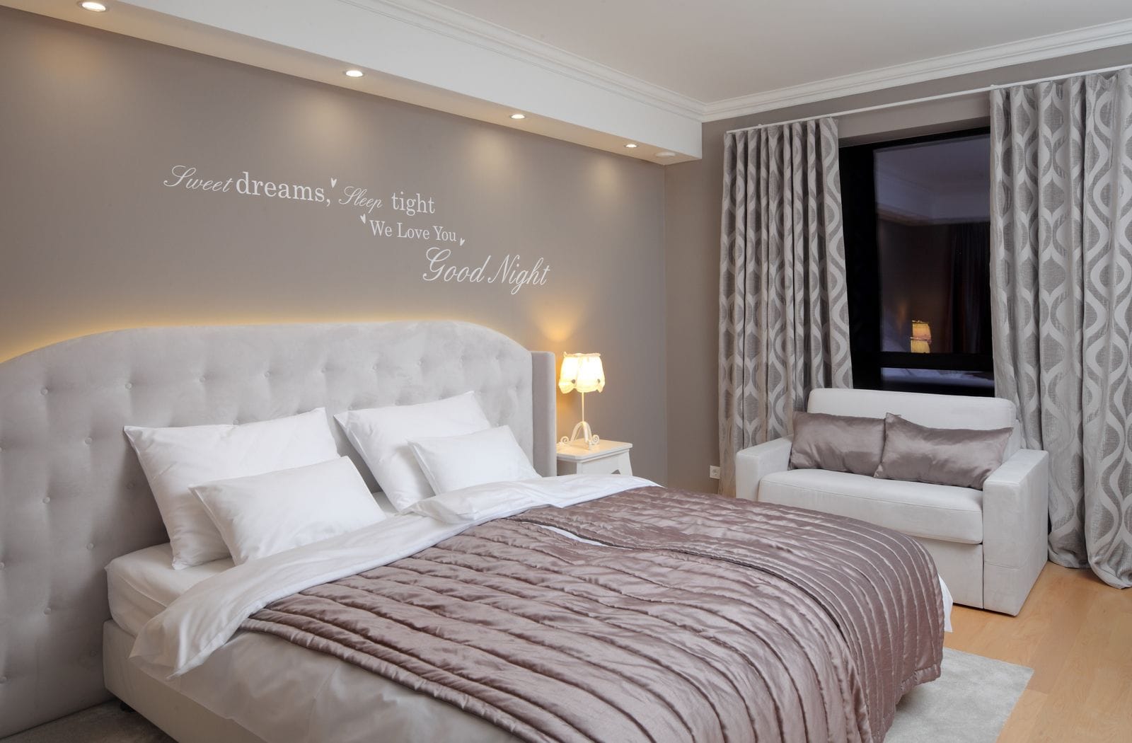 Quarto com cama grande, mesa de cabeceira com abajur, sofá e janela com cortinas.