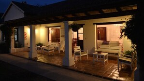 Uma área externa coberta com assentos e uma pequena mesa, provavelmente um alpendre ou espaço de lounge.