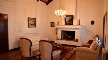 Uma sala de estar com lareira, um candelabro e uma grande janela.