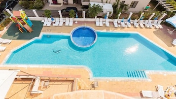 Piscina com um elemento circular central, rodeada por espreguiçadeiras e um parquinho infantil.