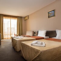 Quarto de hotel com duas camas, uma escrivaninha, uma cadeira, janela com cortinas e um quadro na parede.
