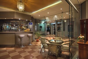 Uma área de bar com banquetas, piso xadrez, mobiliário de vime e uma parede de vidro.